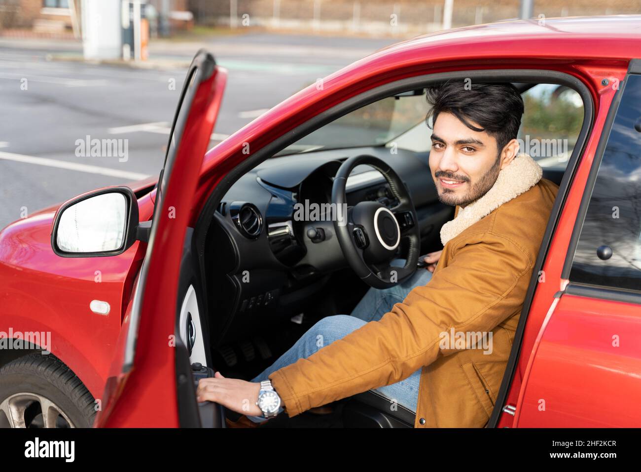 Portrait of young man in jacket opens car door at daytime. View from ...