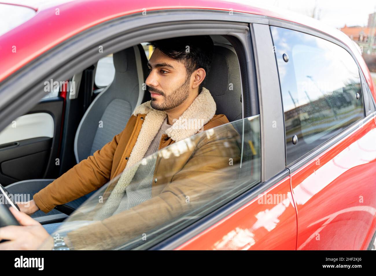 Man in jacket holding driving wheel riding car at daytime. View from ...