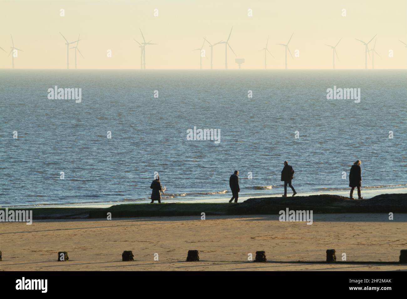 Silhouettes of people on Frinton beach with Gunfleet Sands wind farm on ...