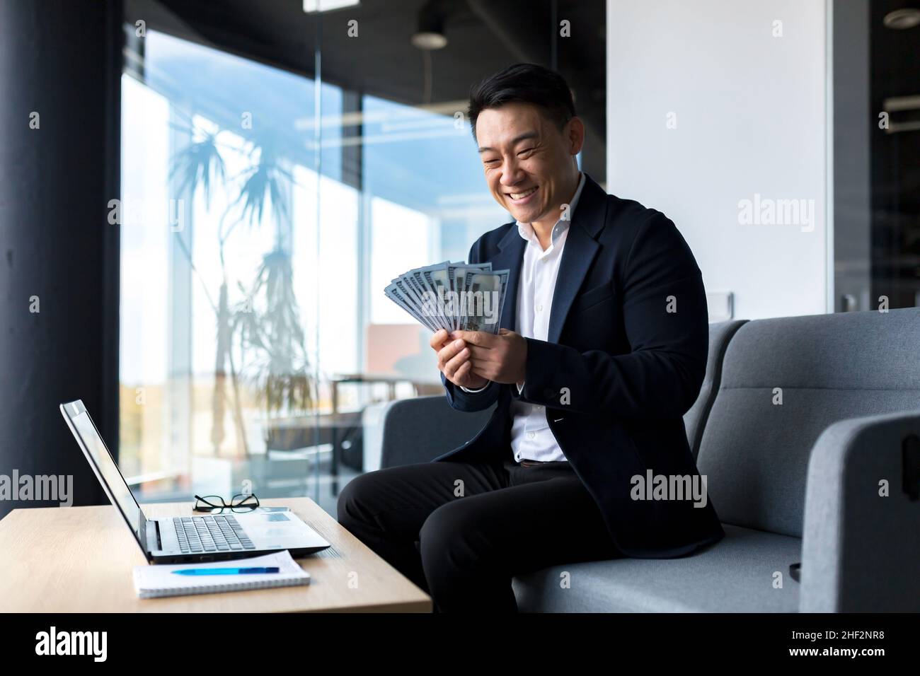 Business owner boss asian, counts cash proceeds sitting in office ...