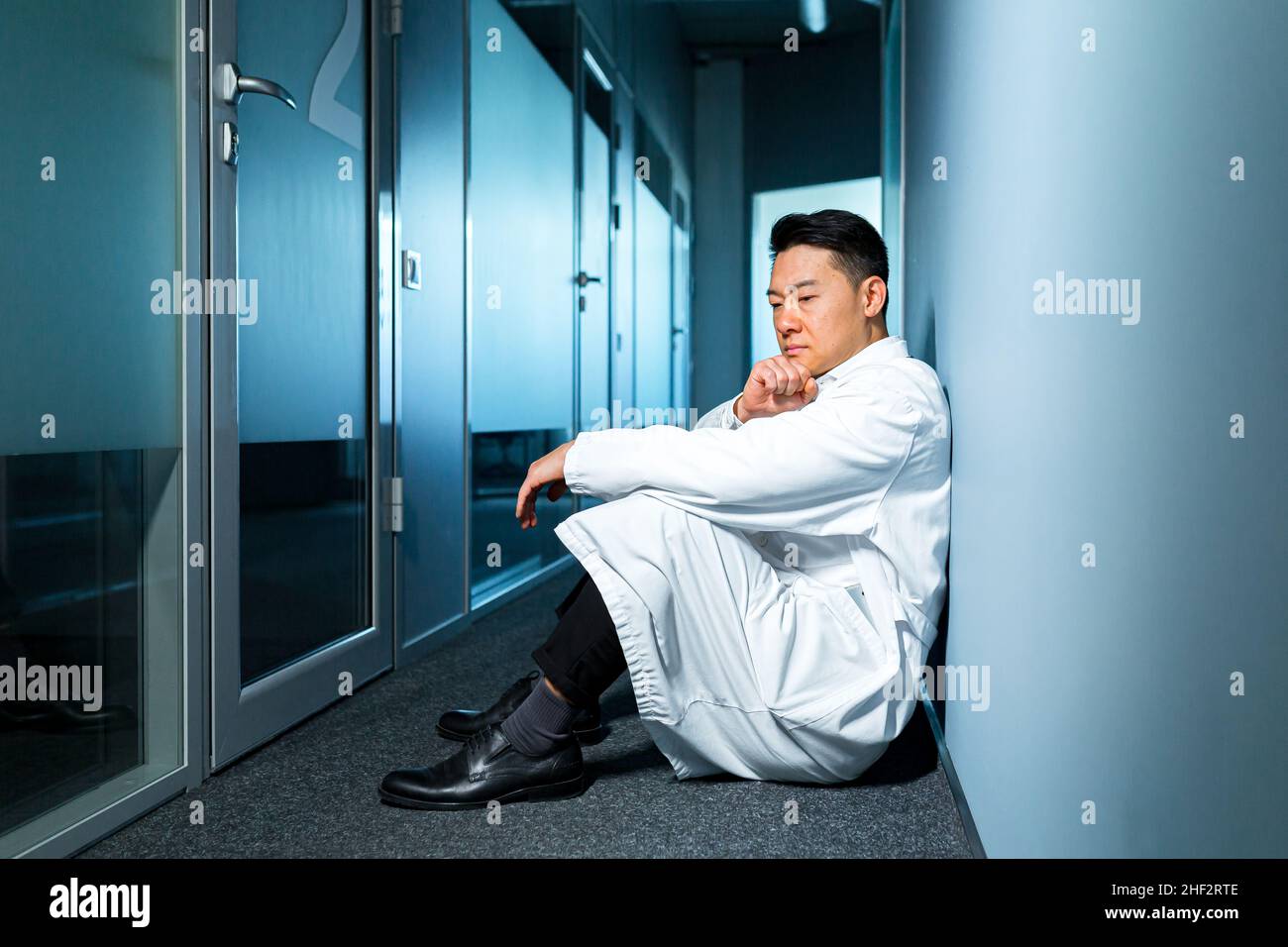 Sad Asian doctor sitting on the floor near the operating room ...
