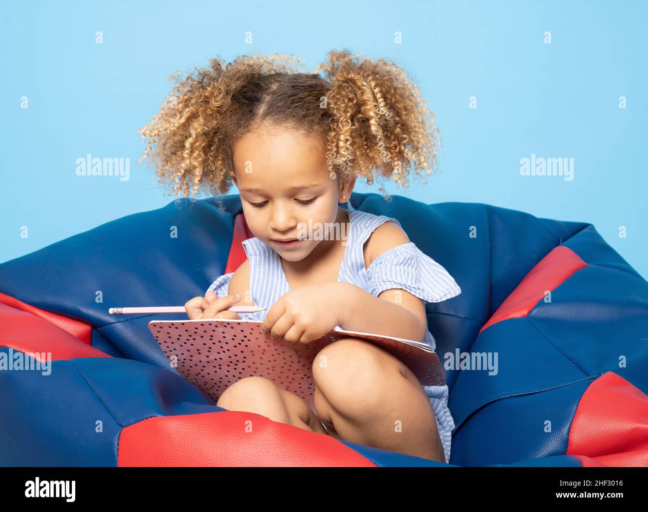 Cute little girl sitting on a big football writing on notebook over ...