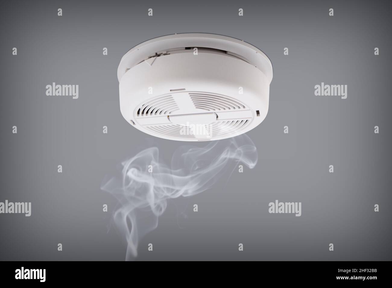 Smoke detector installed on a ceiling with rising smoke underneath ...