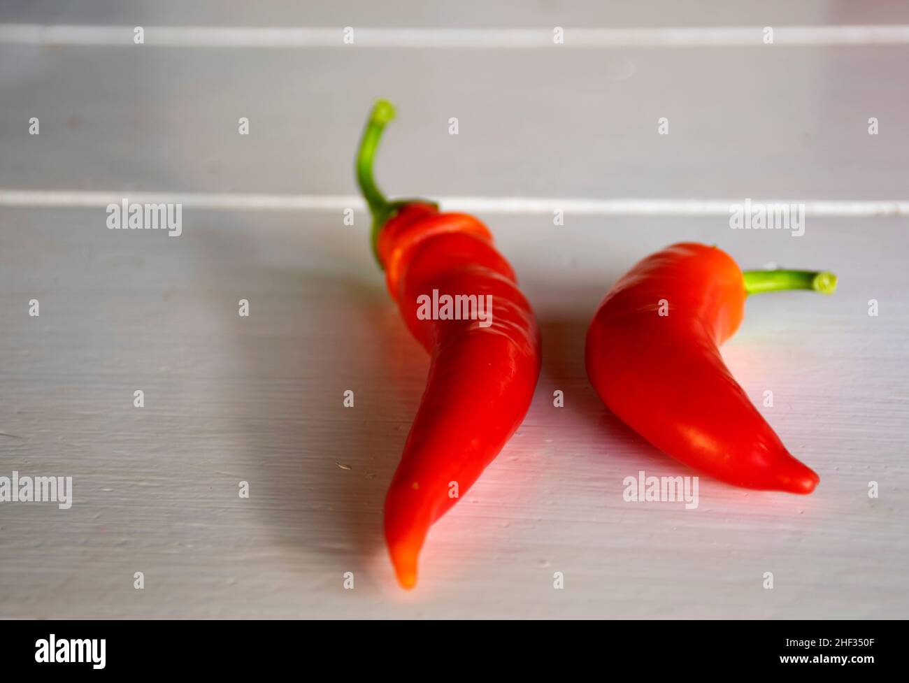 Two red chilli peppers on a white wood background Stock Photo - Alamy