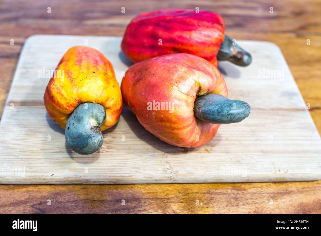 Three cashew apples on a cutting board, their seed pods at the bottom ...