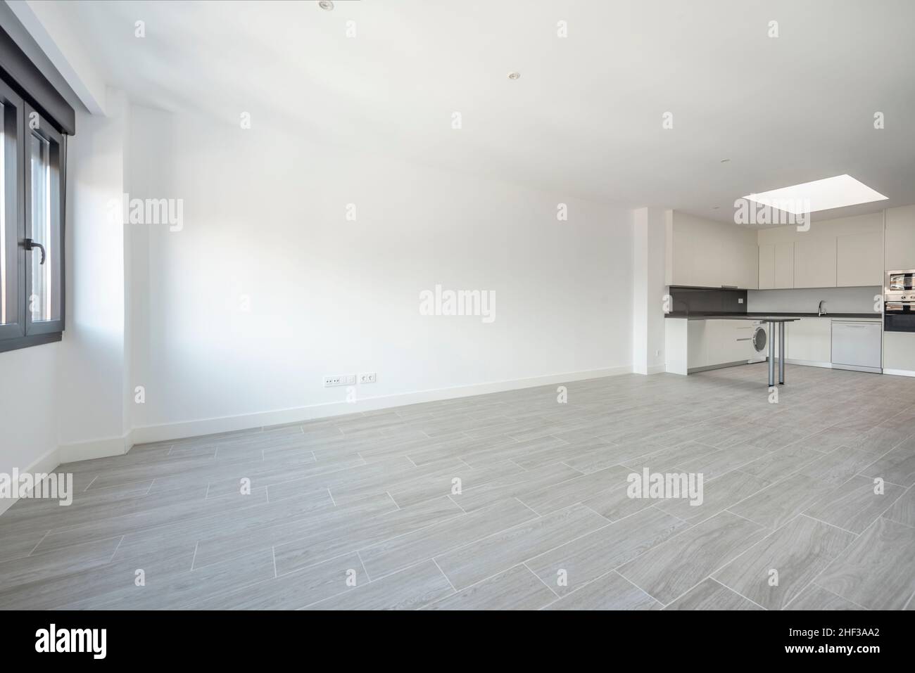 Large empty room with a kitchen at one end and a window at the other ...