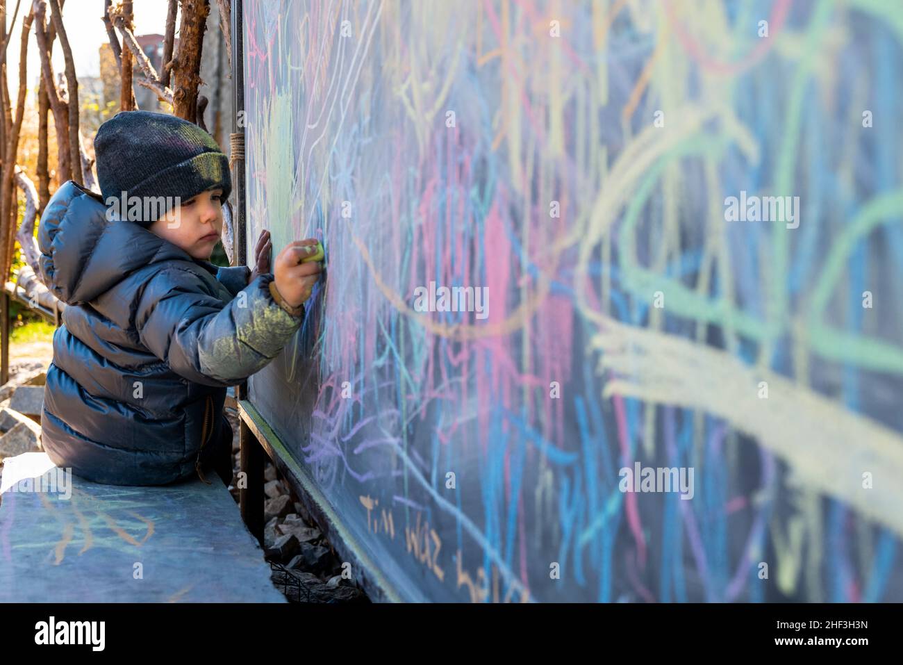 Two year old boy drawing with colorful chalk on city park chalk board ...