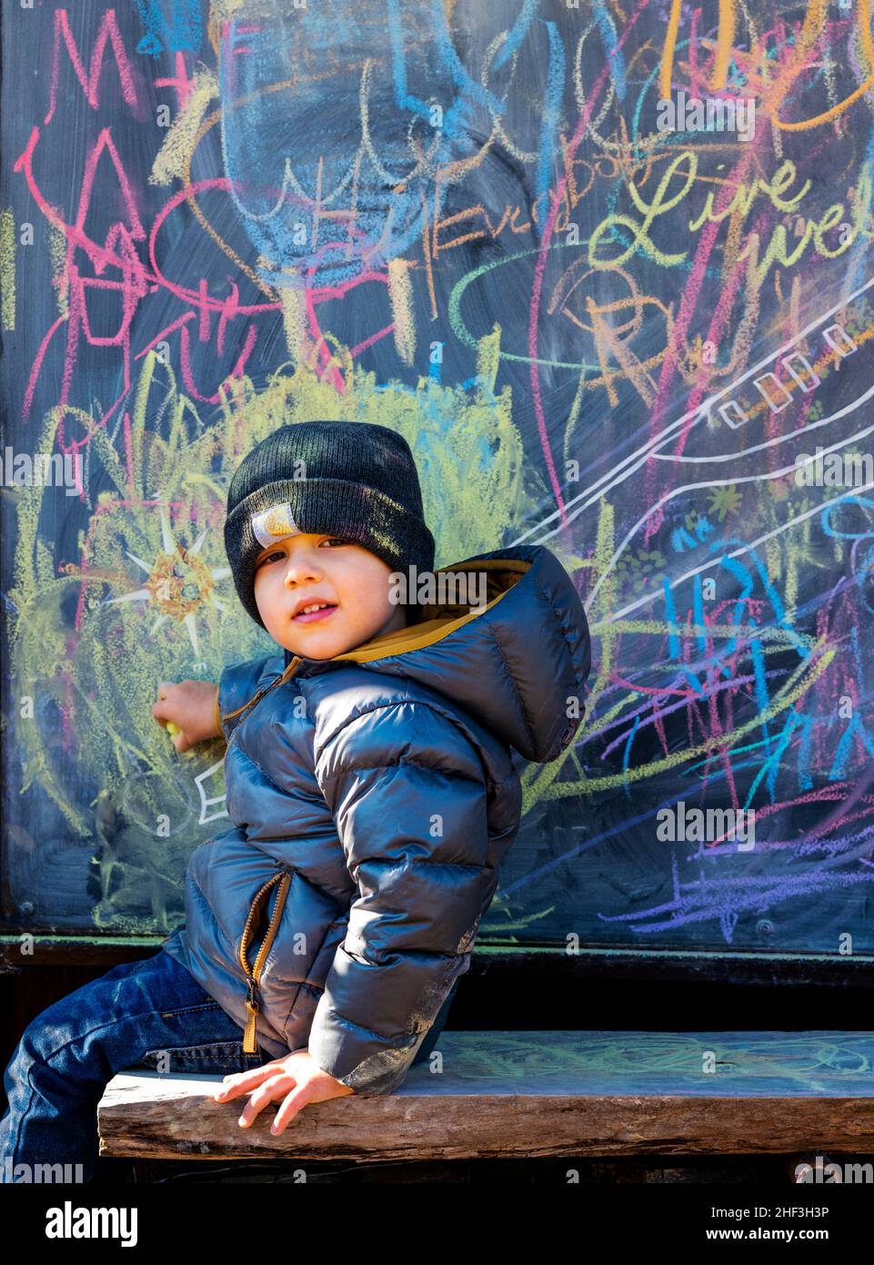 Two year old boy drawing with colorful chalk on city park chalk board ...