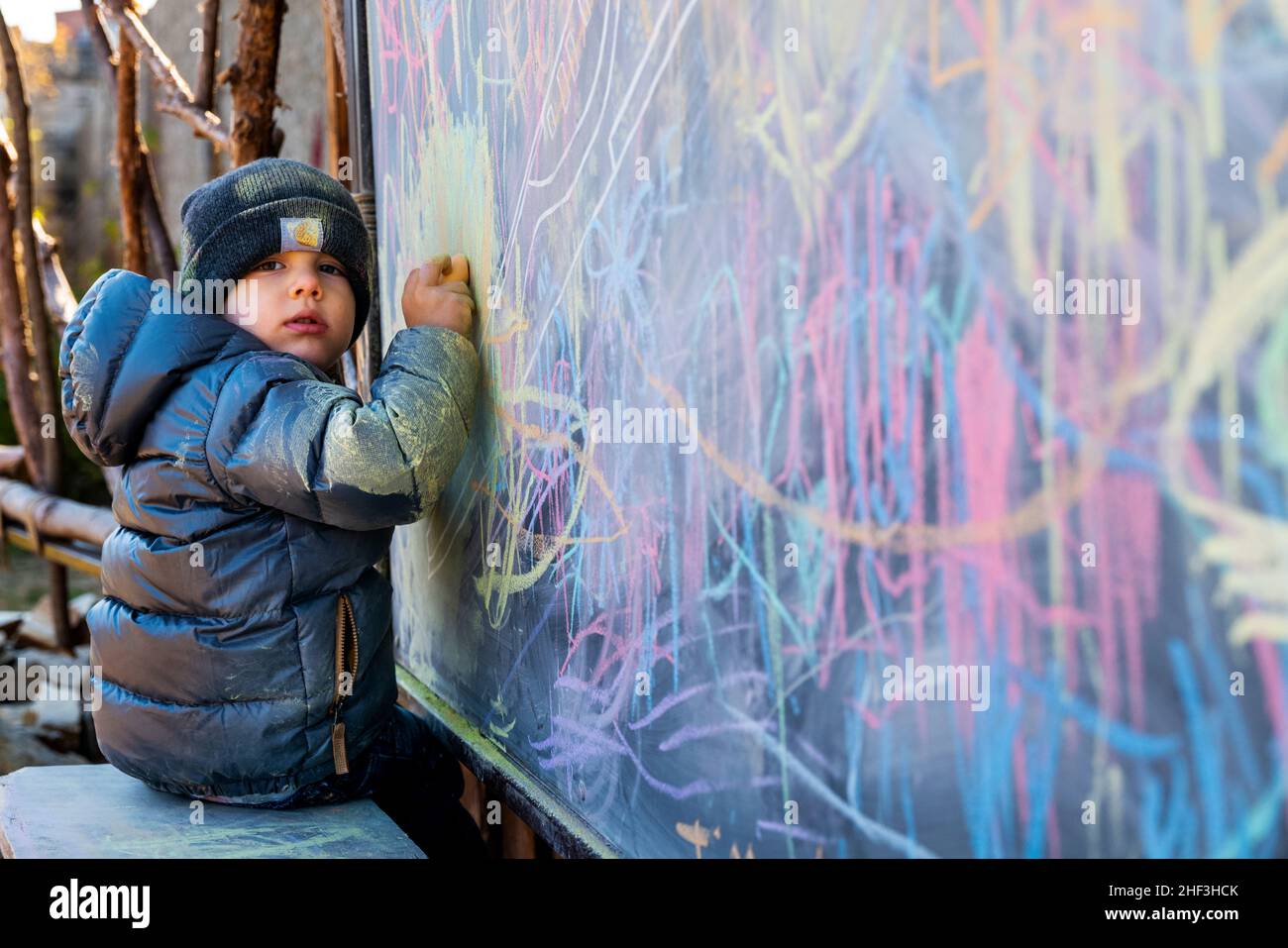 Two year old boy drawing with colorful chalk on city park chalk board ...
