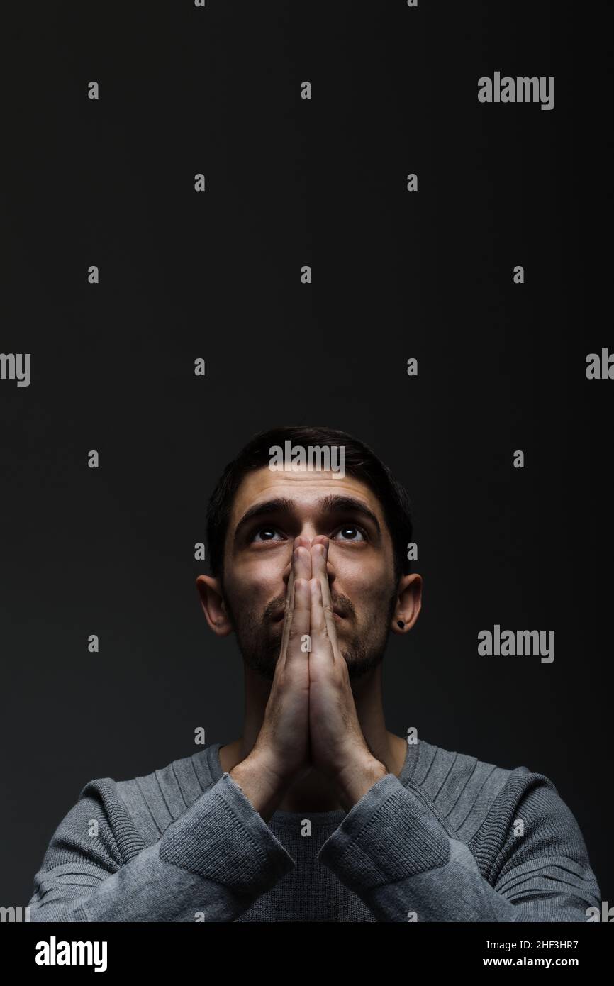 Headshot of serious confident young man praying in dark room. Lit from ...