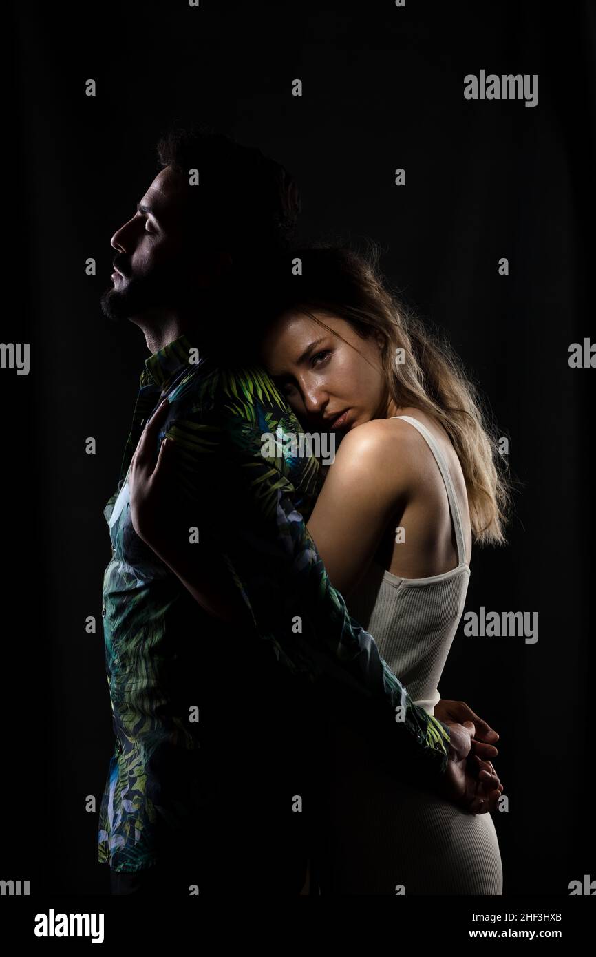 Couple posing on black background. Girl hugging boy in shadow from ...