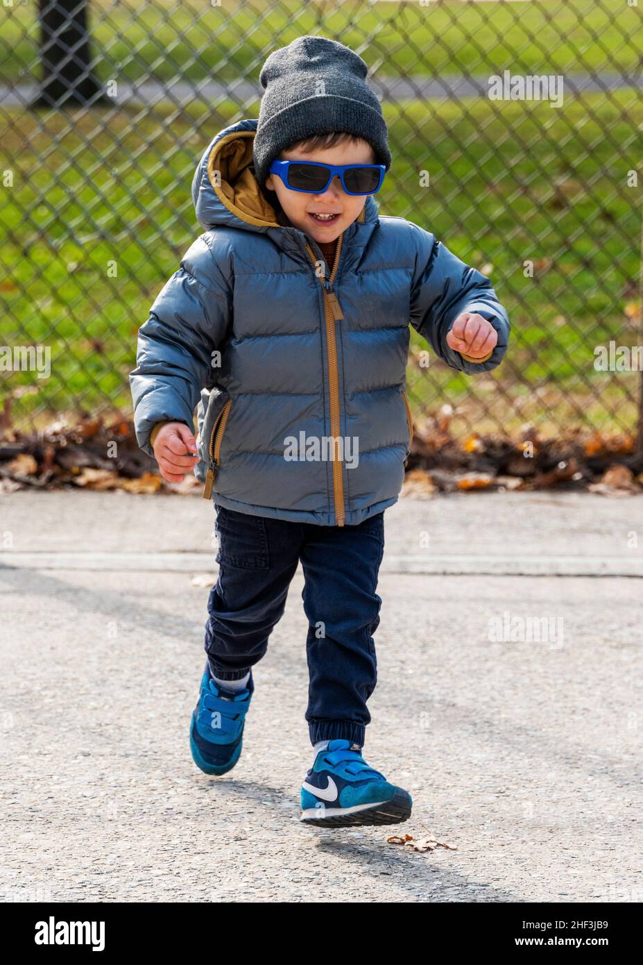 Two year old boy with sunglasses running on city park playground ...