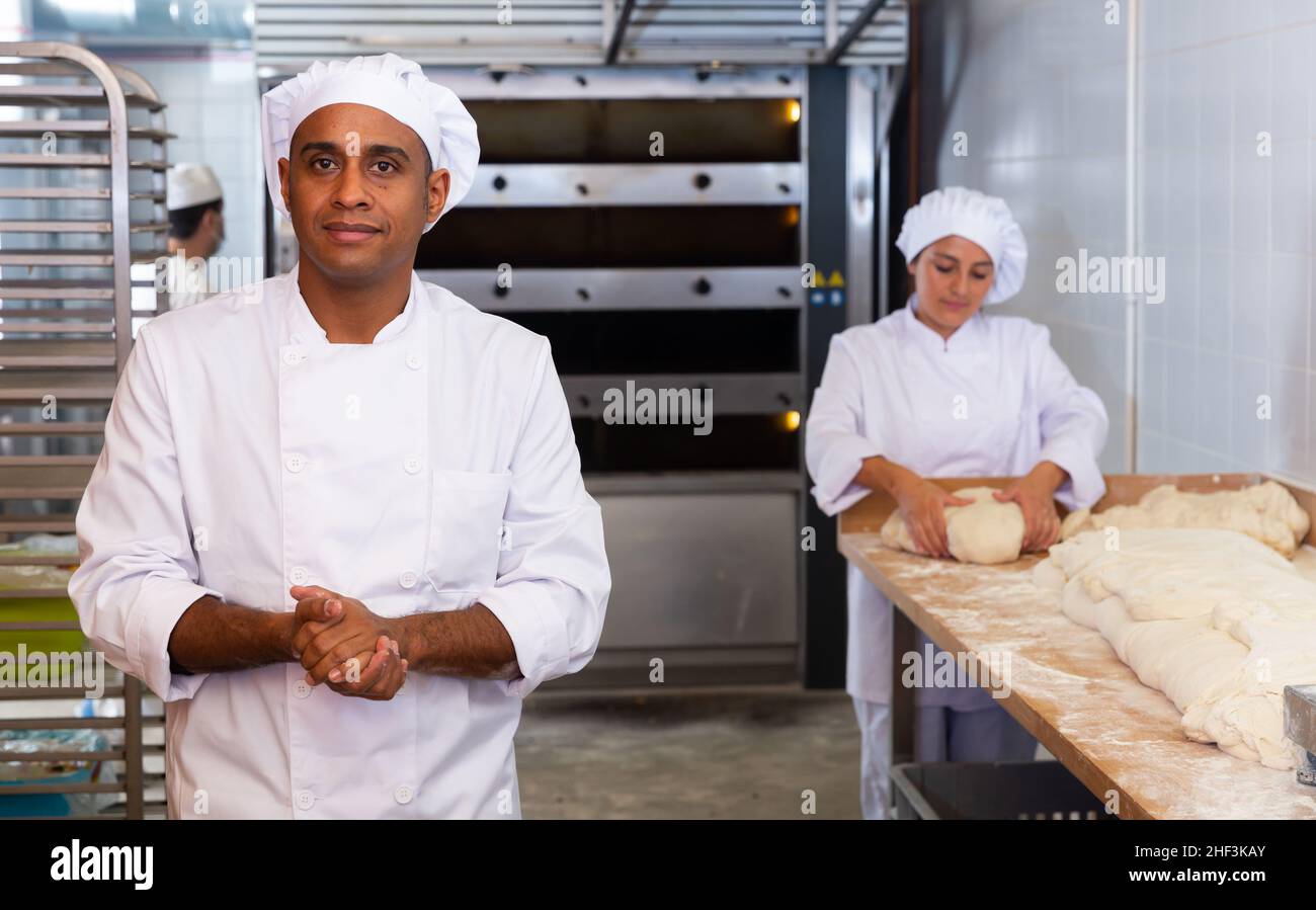 Confident bakery owner posing against busy workers background Stock ...