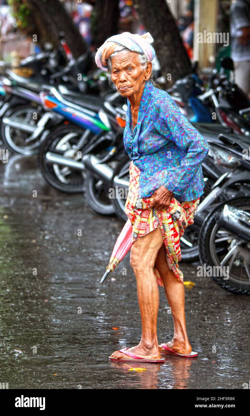 An old Balinese woman dressed in batik walking in a street at Sukawati ...