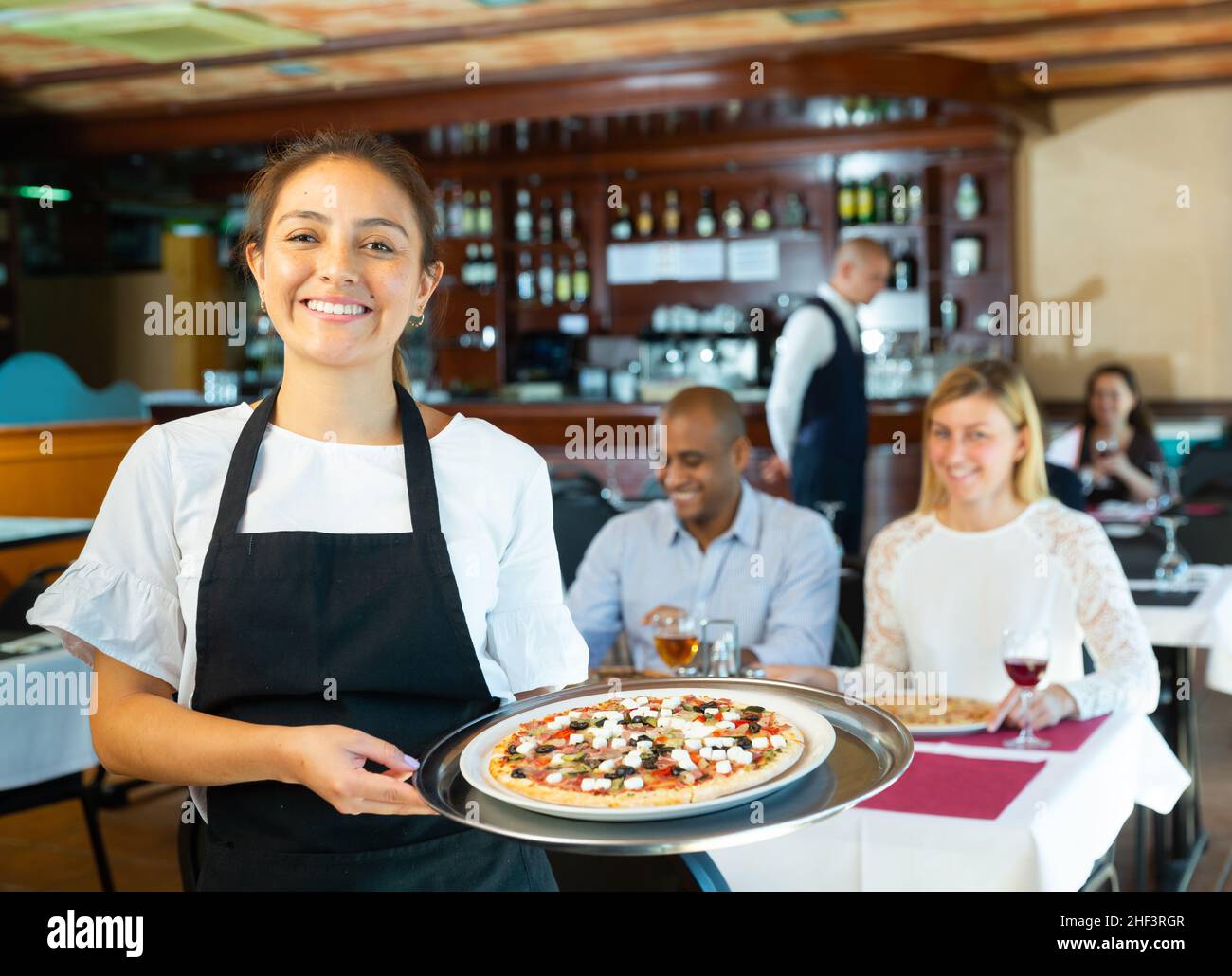 Hospitable latin american waitress meeting guests in pizzeria Stock ...