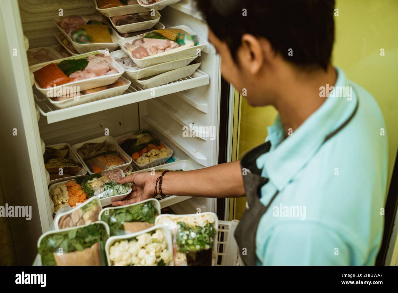 Male vegetable seller putting packaged vegetables into the refrigerator ...