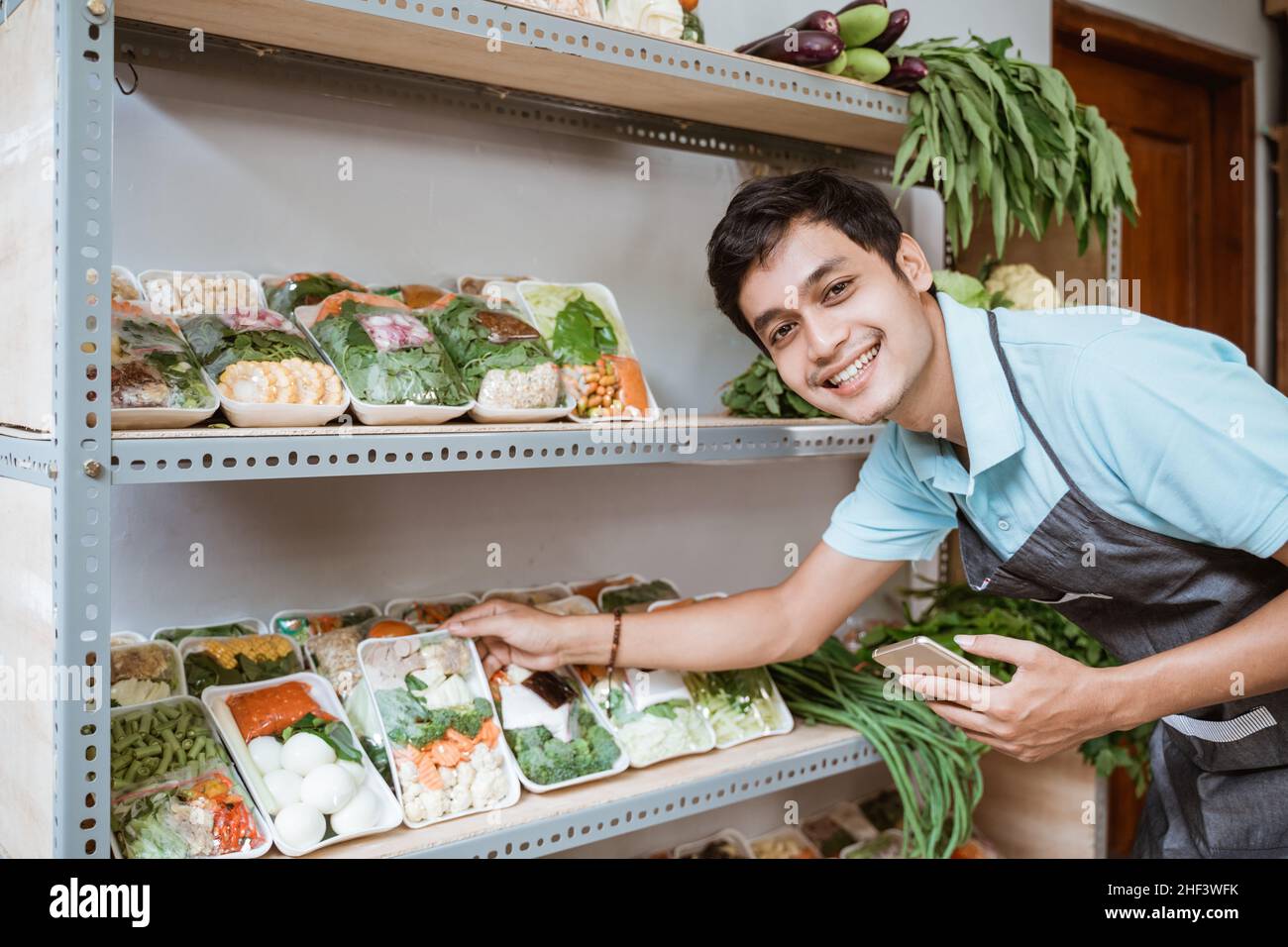 Smiling man selling vegetables holding a cell phone while checking ...
