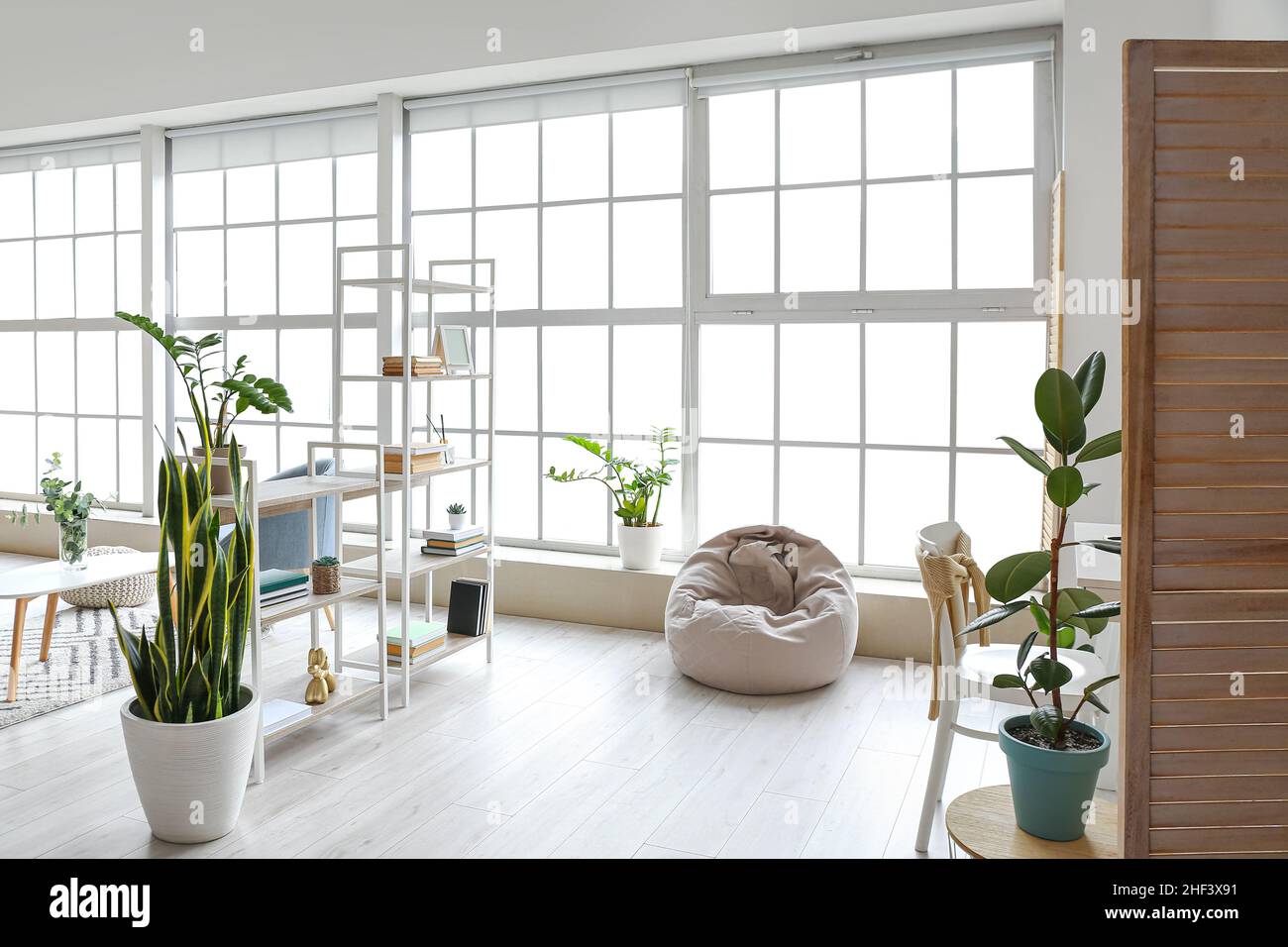 Comfy pouf and modern bookshelf with decor near window Stock Photo - Alamy