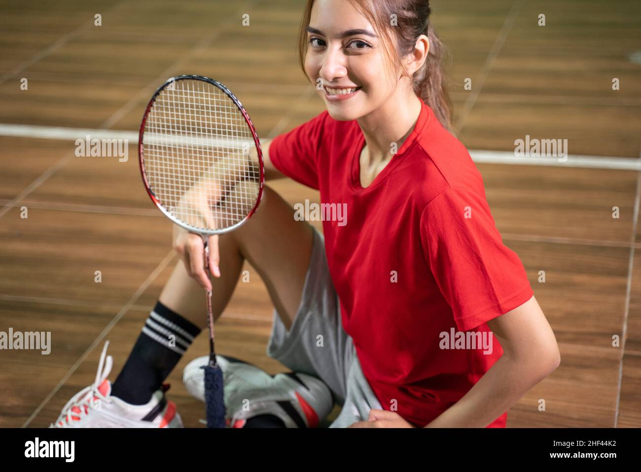 Beautiful smiling female badminton player sitting with holding racket ...