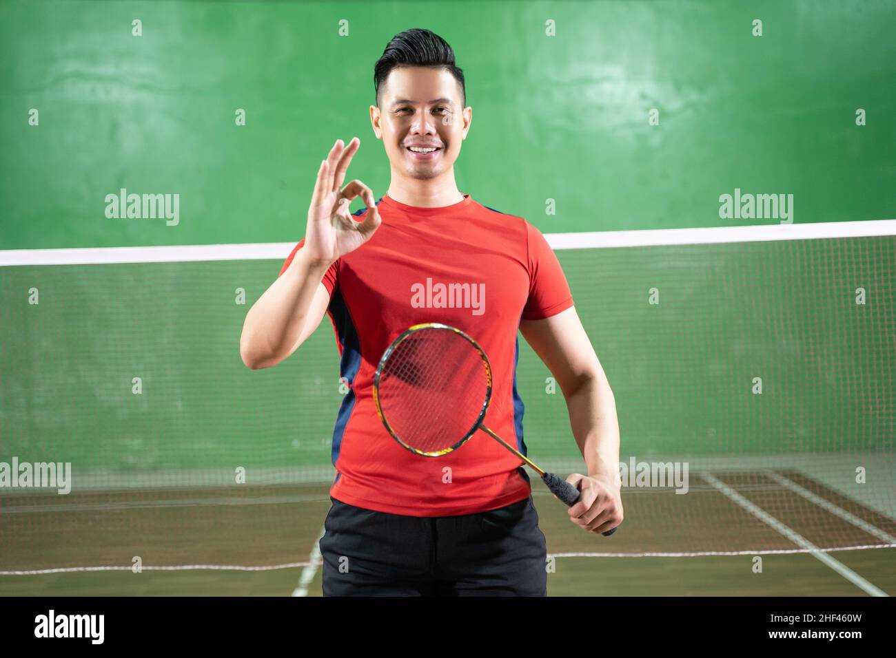 Smiling male badminton player holding racket with okay hand gesture ...