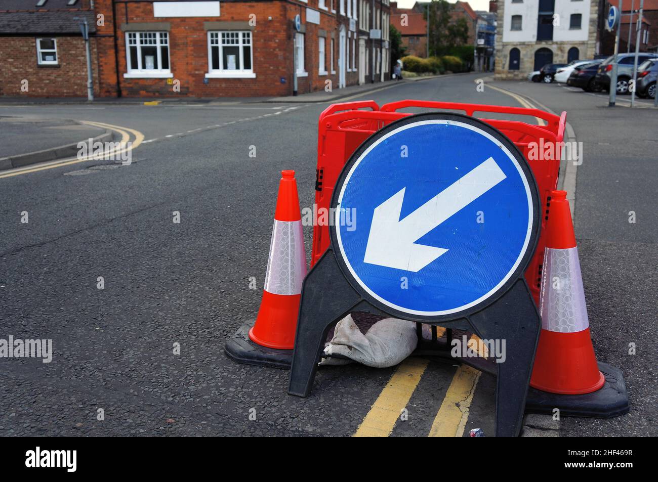 white and blue arrow warning sign on the roadside with defocused street ...