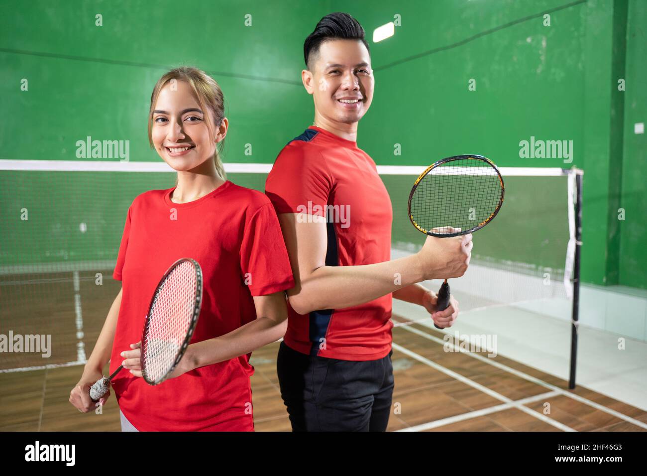 Two smiling badminton players holding rackets standing back to back ...