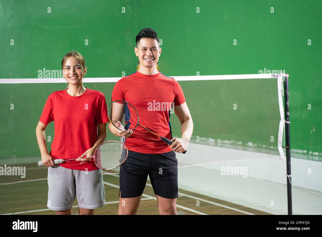 Two confident badminton players holding rackets standing against net ...