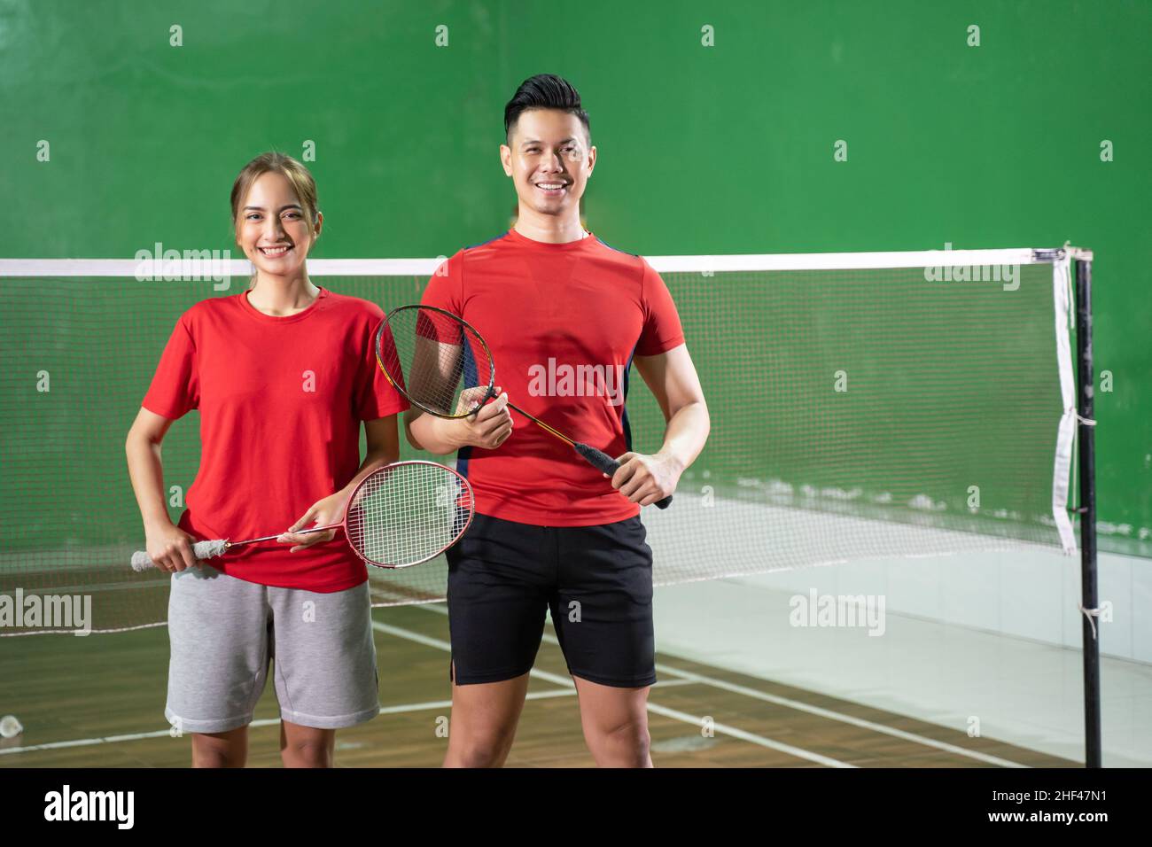 Two smiling badminton players holding rackets standing against net ...