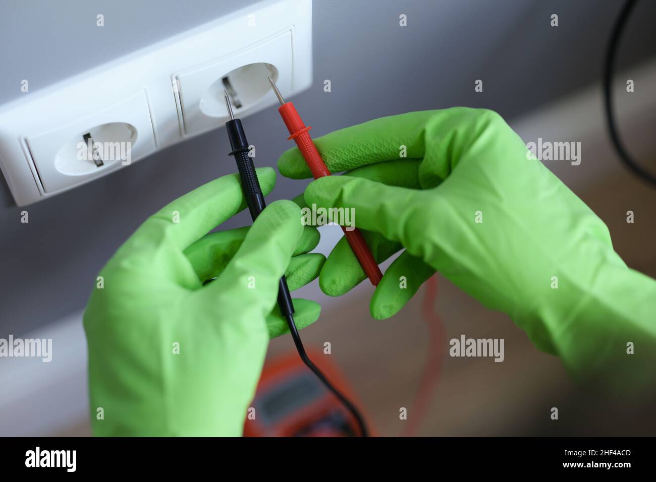 Hands in green gloves plug voltmeter into an outlet in wall Stock Photo ...