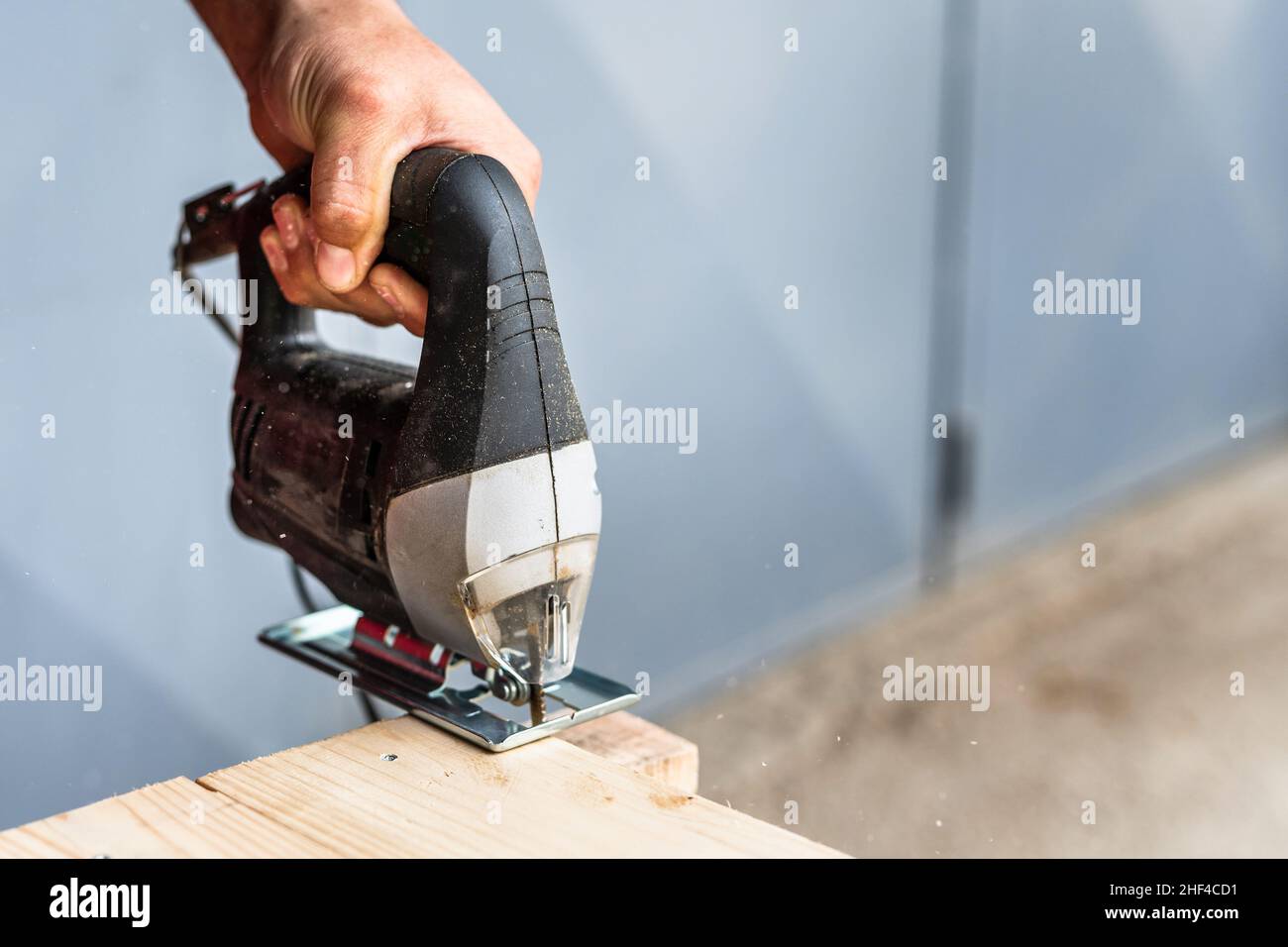 Close up on hand of unknown carpenter working with an electric jigsaw ...
