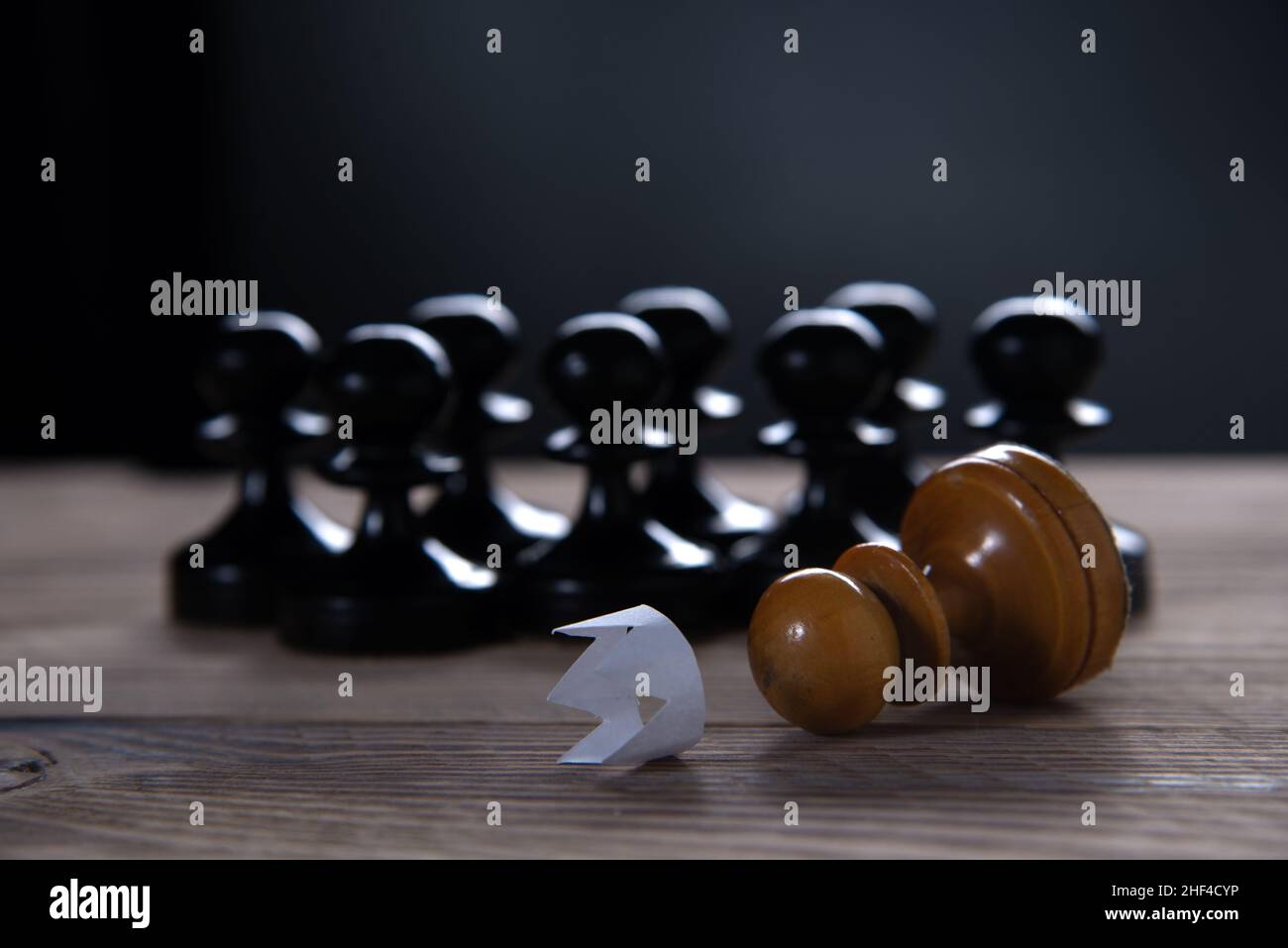 A lone white pawn with a discarded paper crown lies surrounded by many ...