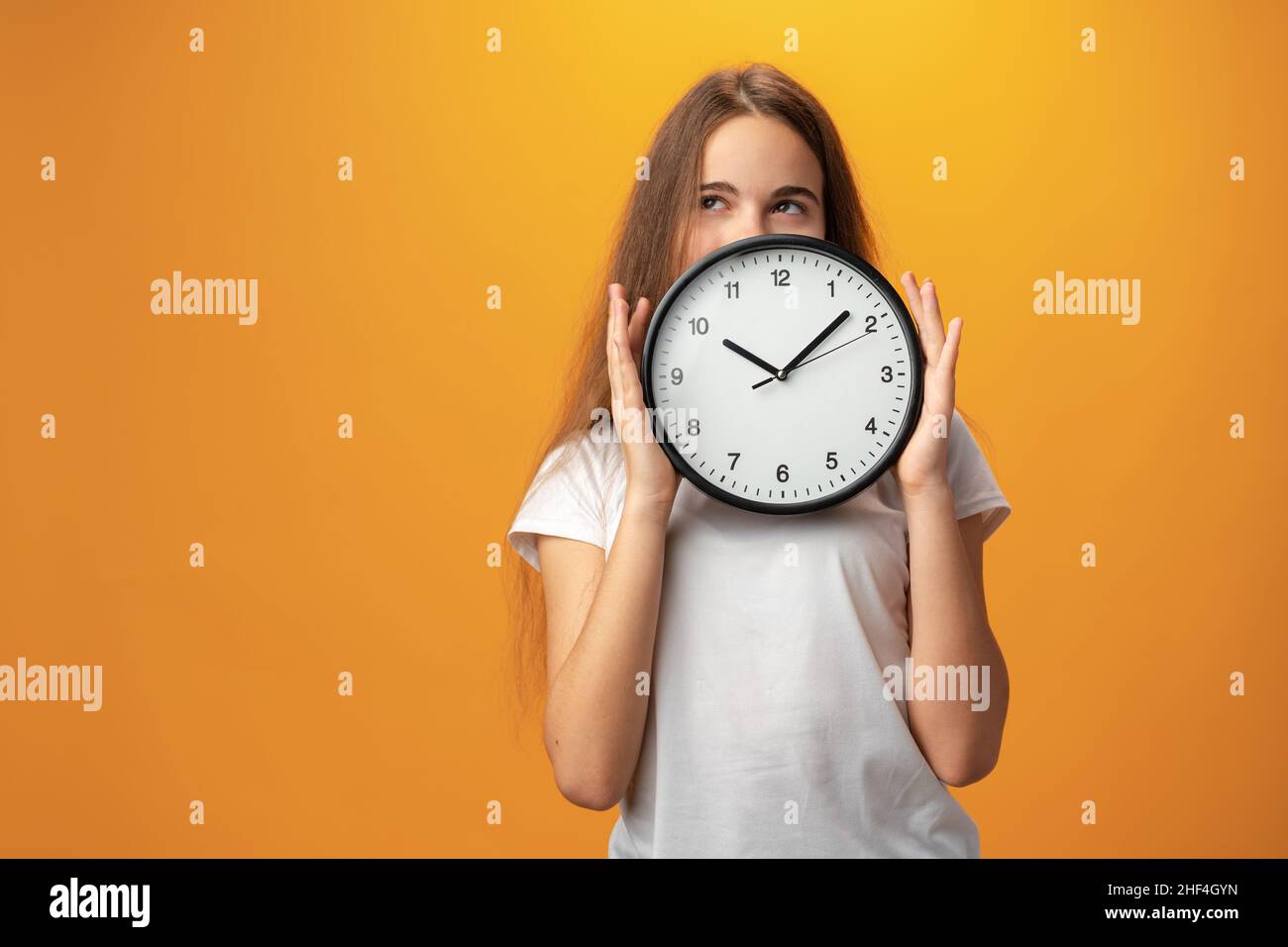 Beautiful teen girl holding wall clock over yellow background Stock ...