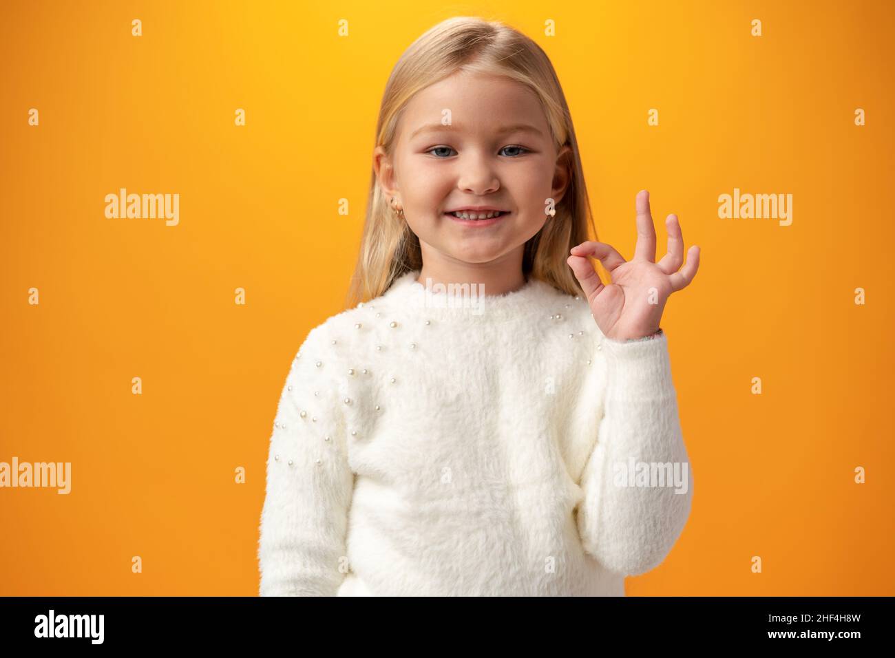 Portrait of positive kid girl show okay sign over yellow background ...