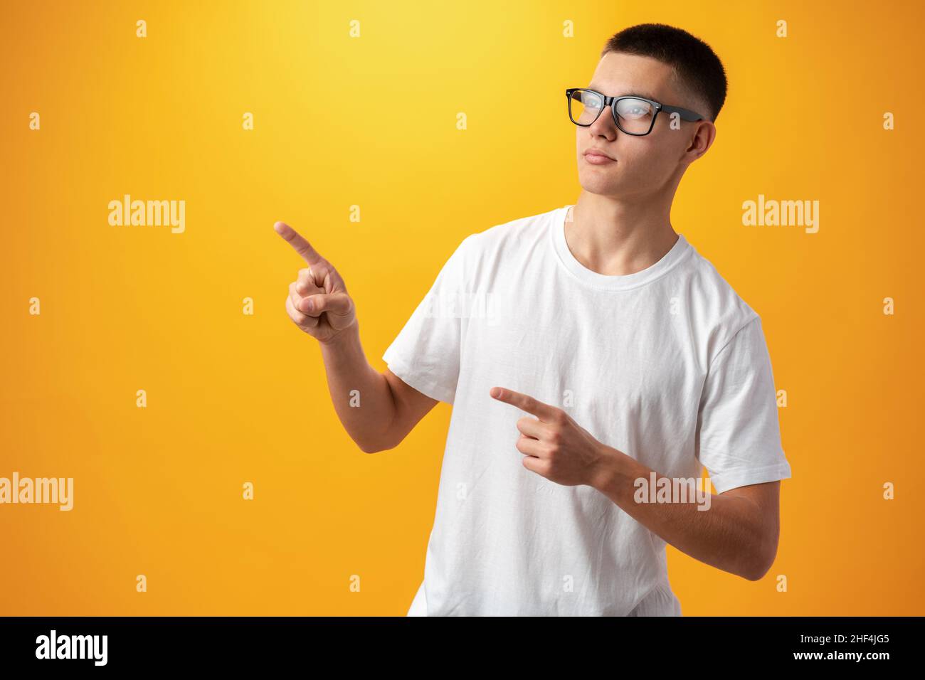 Portrait of teen boy pointing fingers away at copyspace against yellow ...