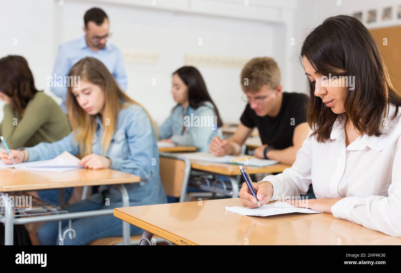 Young girl is writing test and thinking about questions at the desk ...