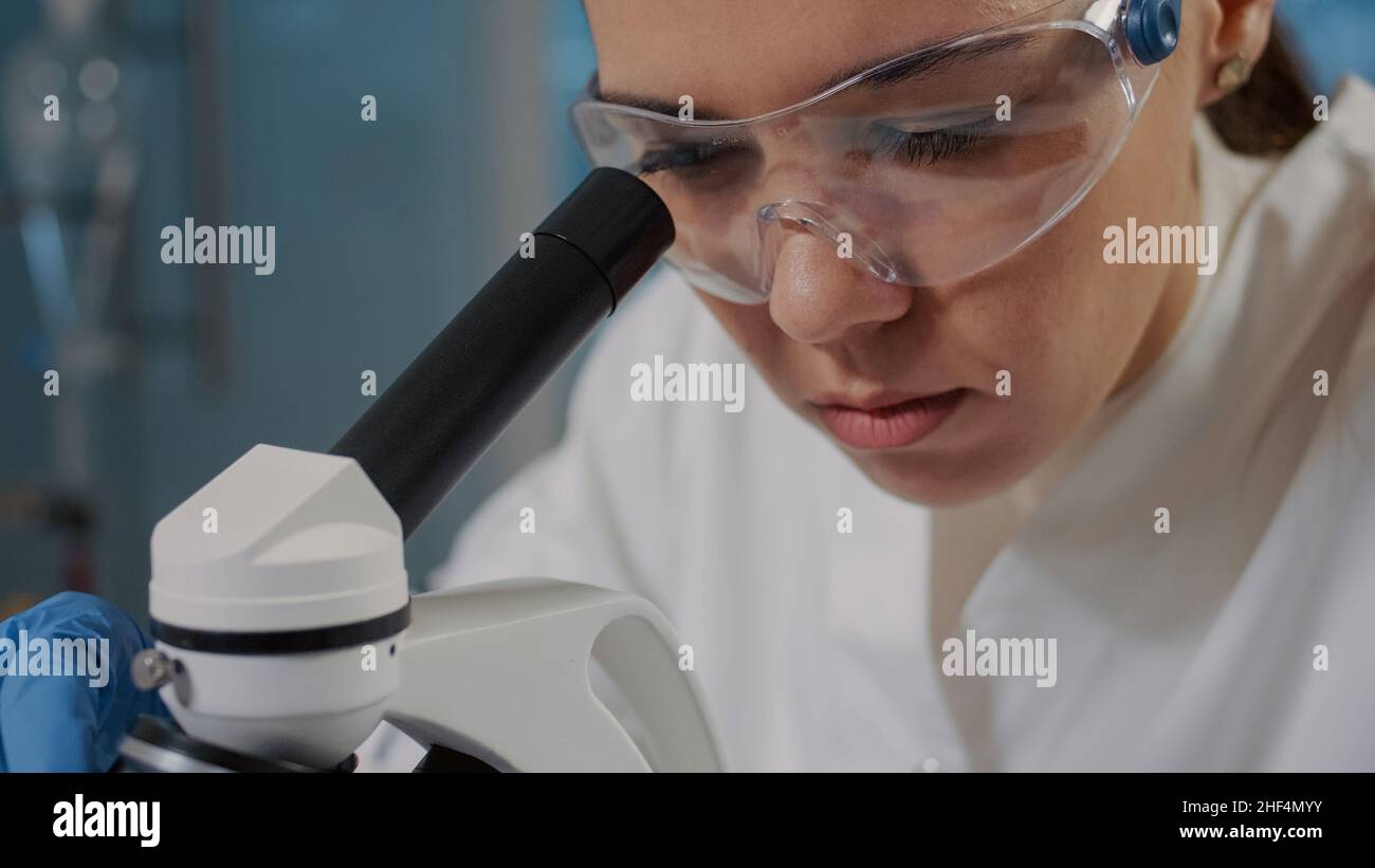 Woman looking through microscope lens to analyze dna sample in ...