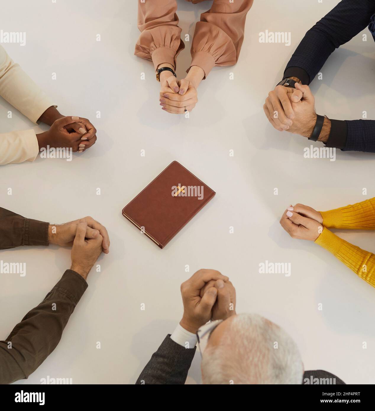 Diverse people sitting around table with the Holy Bible and praying to ...