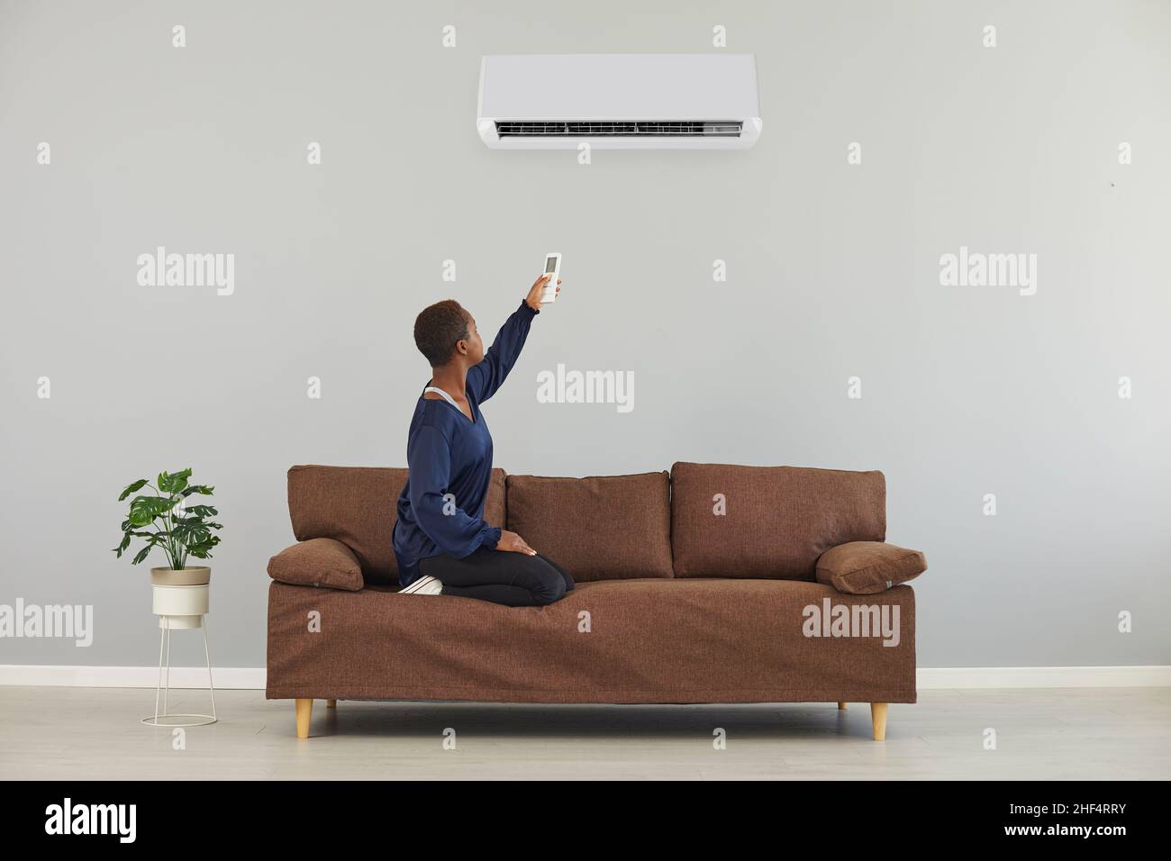 Woman on the sofa using a remote control to set the temperature on the ...