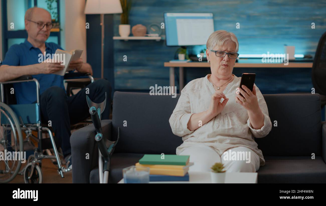 Senior person holding smartphone to talk on teleconference call at home ...