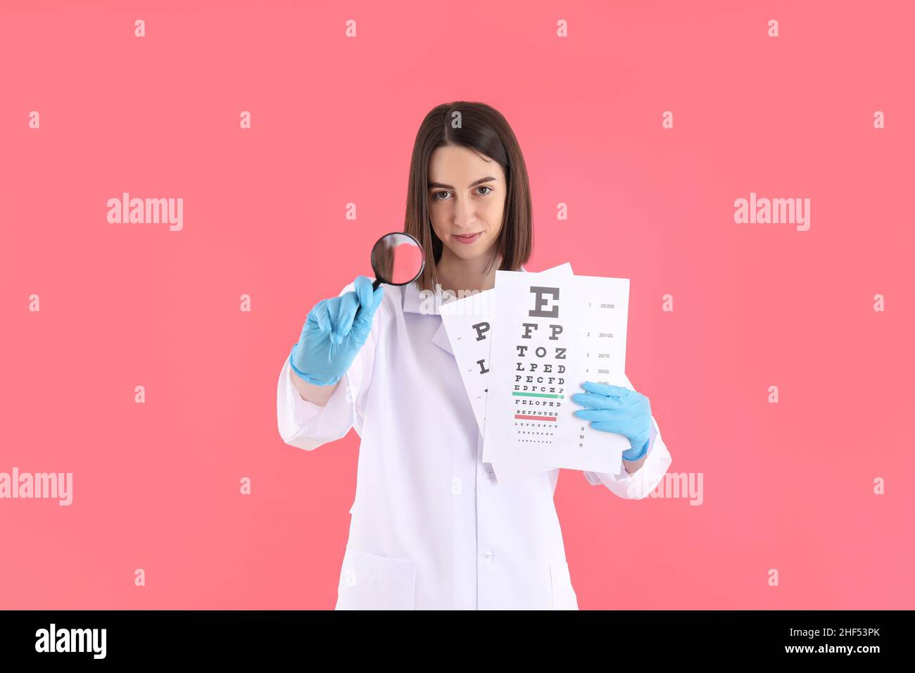 Female trainee doctor with vision test and magnifier on pink background ...