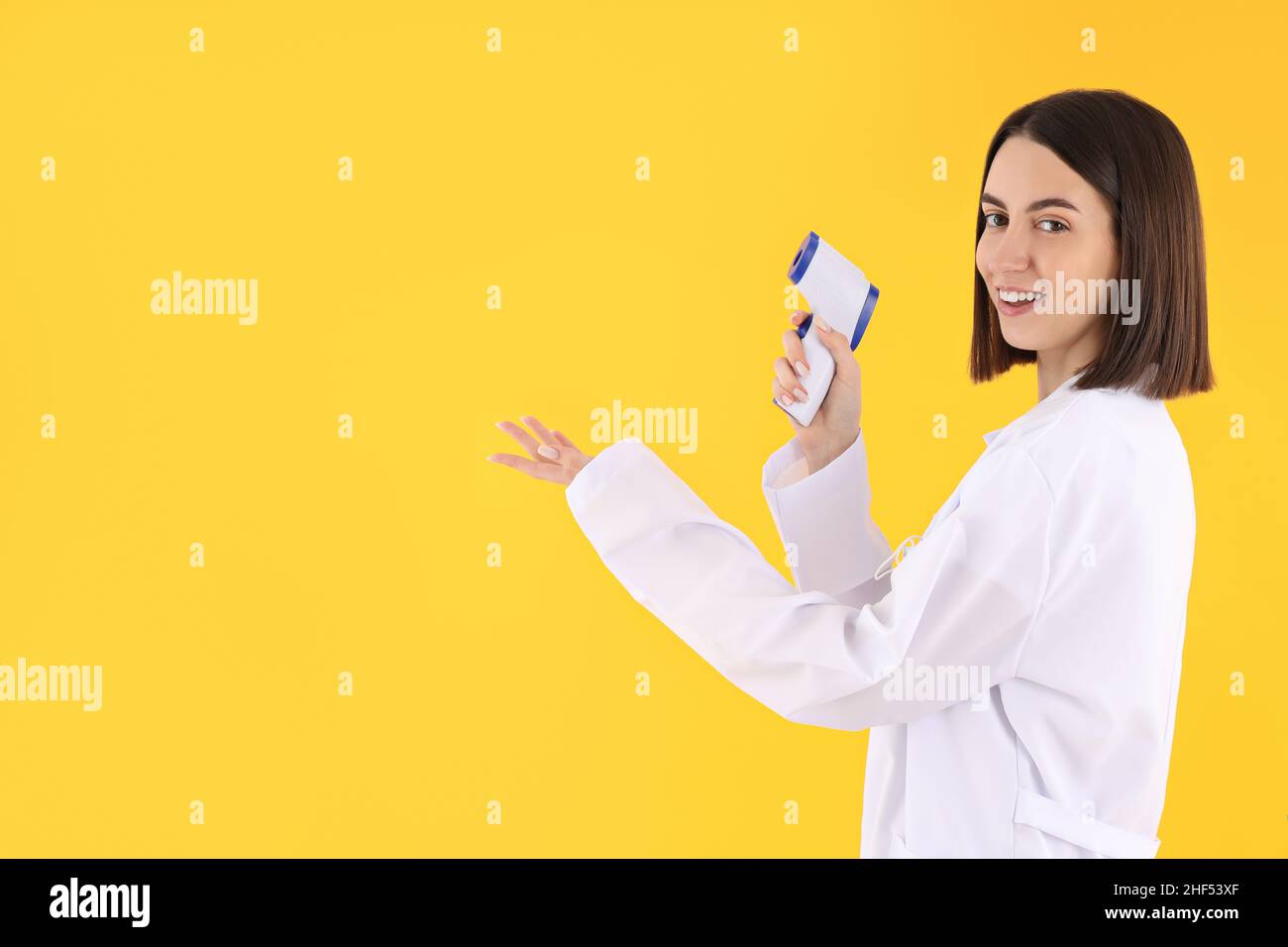 Female trainee doctor with thermometer gun on yellow background Stock ...