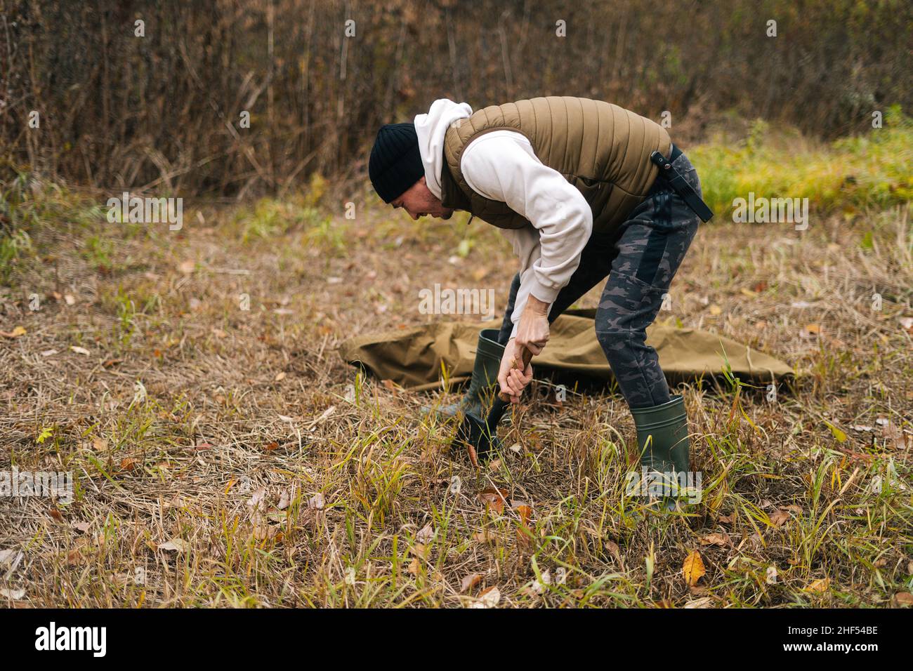 Focused tourist male wearing warm clothes digging fire place using ...