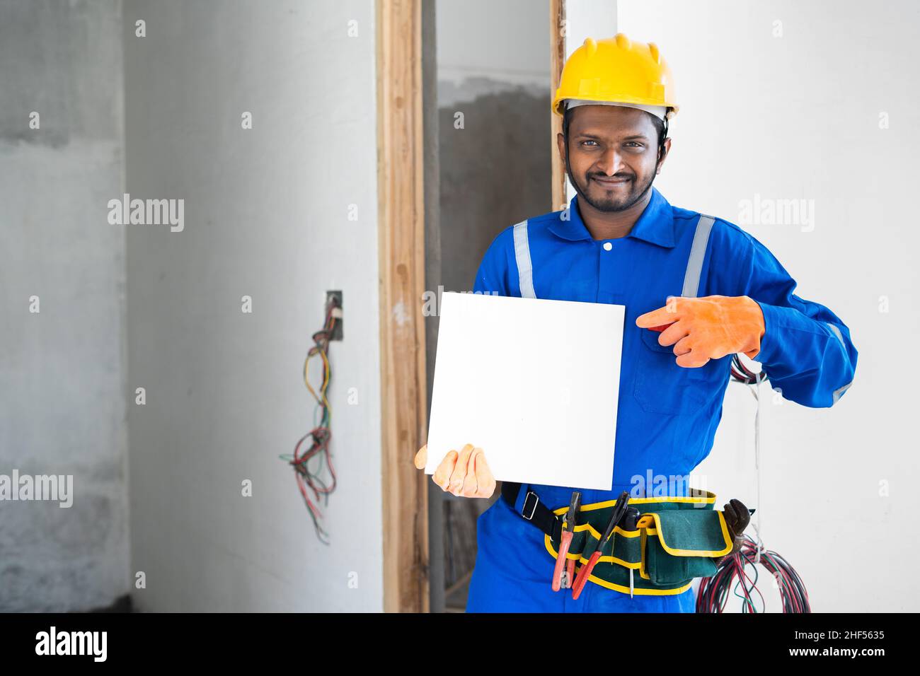 Smiling plumber showing empty white sign board by pointing finger at ...