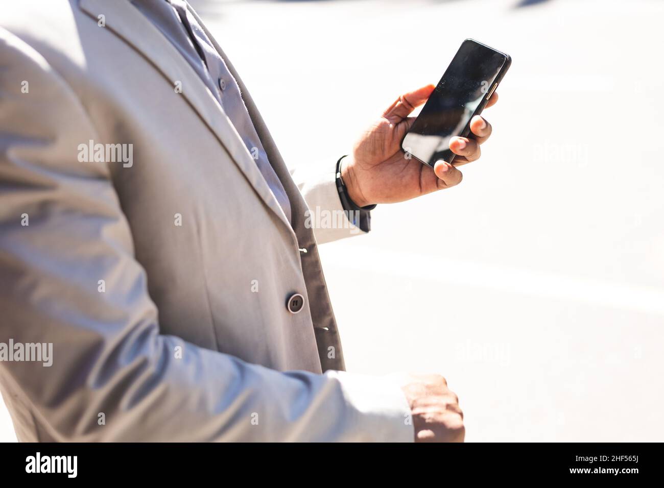 Mid section of businessman with suitcase using smartphone on the street ...