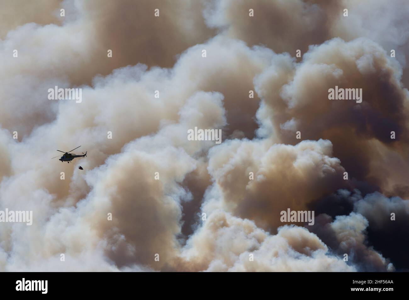 A fire helicopter with a bambi bucket in the clouds of a forest fire ...
