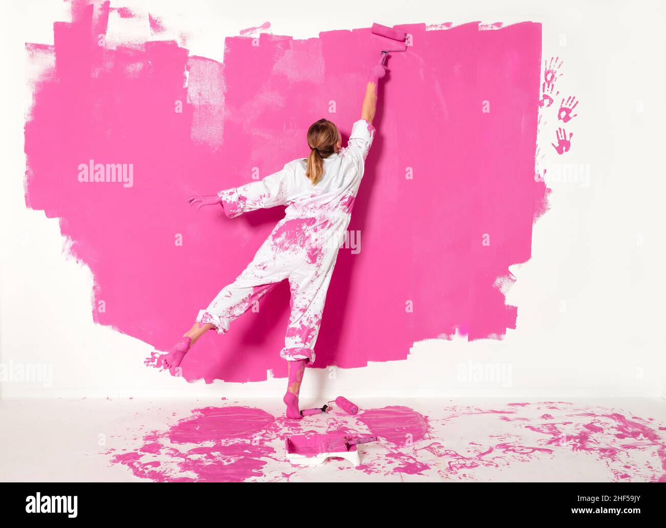 Young girl painting a wall with pink color. She is wearing working ...