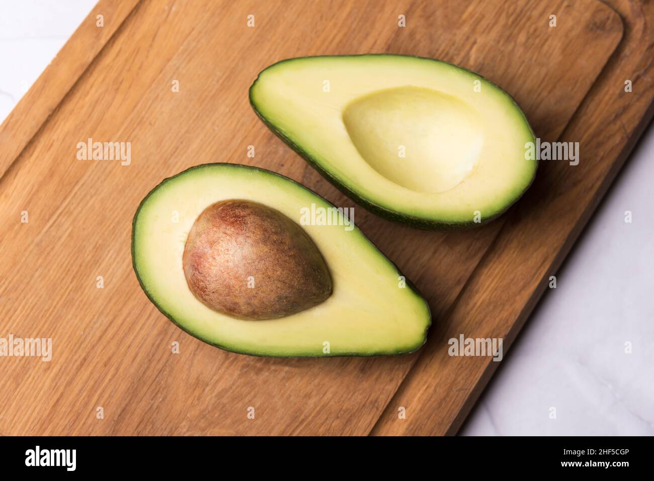 Two avocado parts on wooden desk, cut to half, seed visible Stock Photo ...