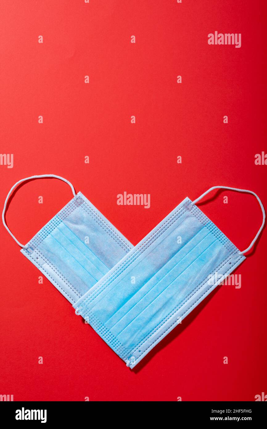 Overhead view of protective face masks arranged in heart shape on red ...