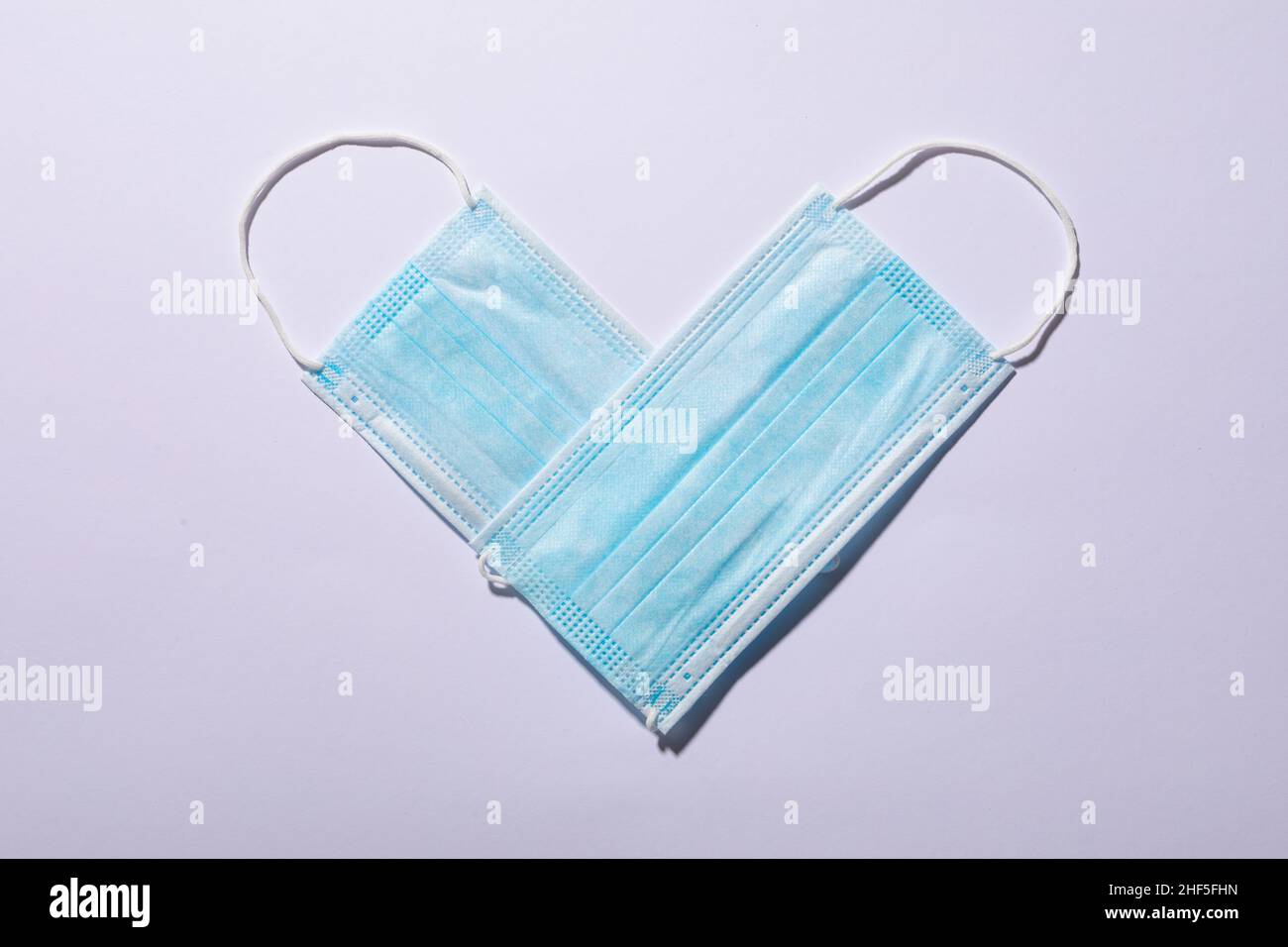 Overhead view of protective face masks arranged in heart shape on white ...