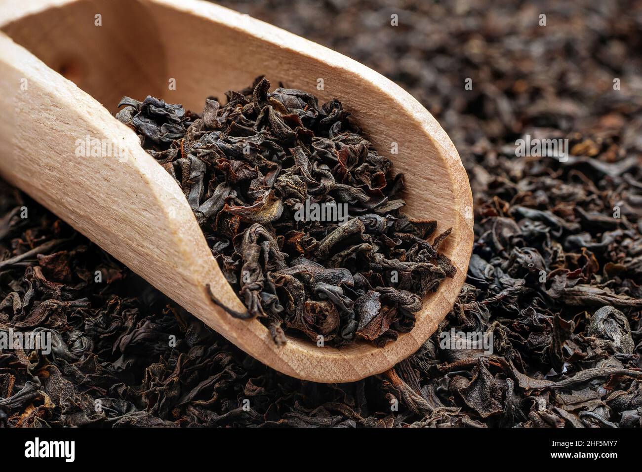 Dry long leaf tea in wooden scoop. Macro of loose black tea Stock Photo ...